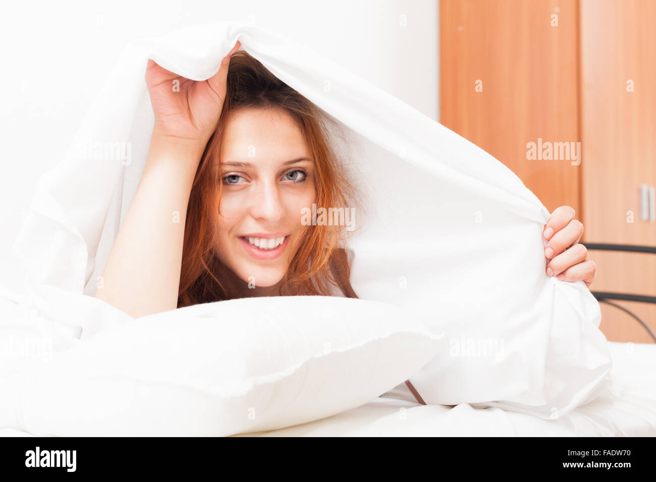 Red-haired young woman waking up on white sheet in bed at home Stock ...