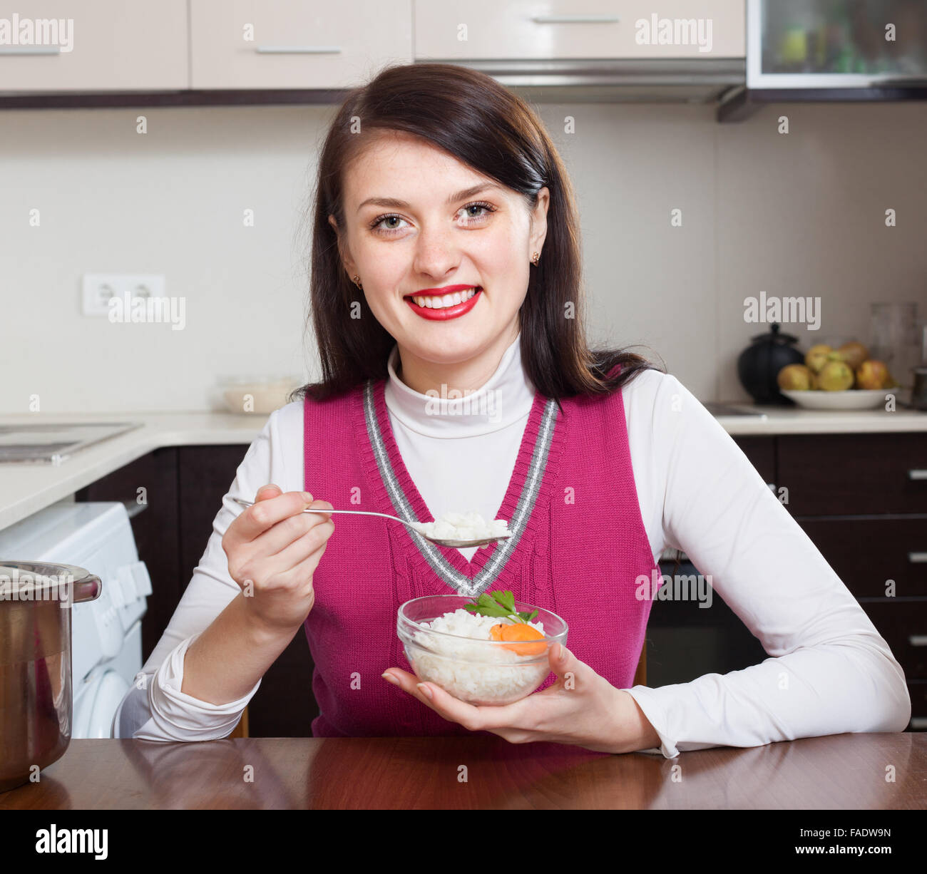 Smiling brunette woman eating boiled rice at table Stock Photo - Alamy