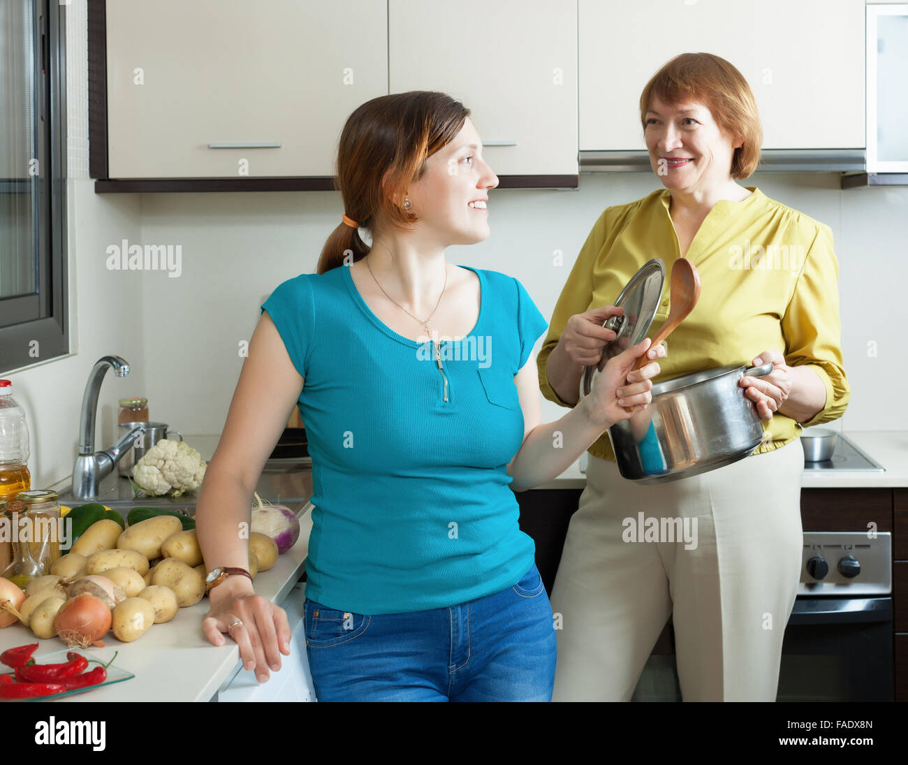 Positive young woman and mature mother cooking lunch in kitchen at home ...