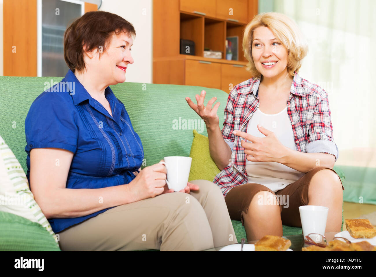 Two happy colleagues in years drinking tea and chatting during coffee ...