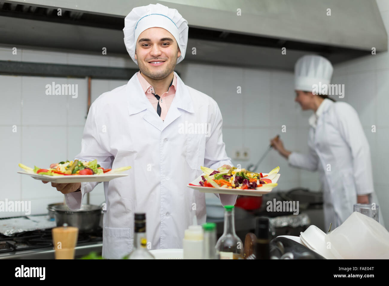Positive chef with assistant cooking at kitchen in the restaurant ...