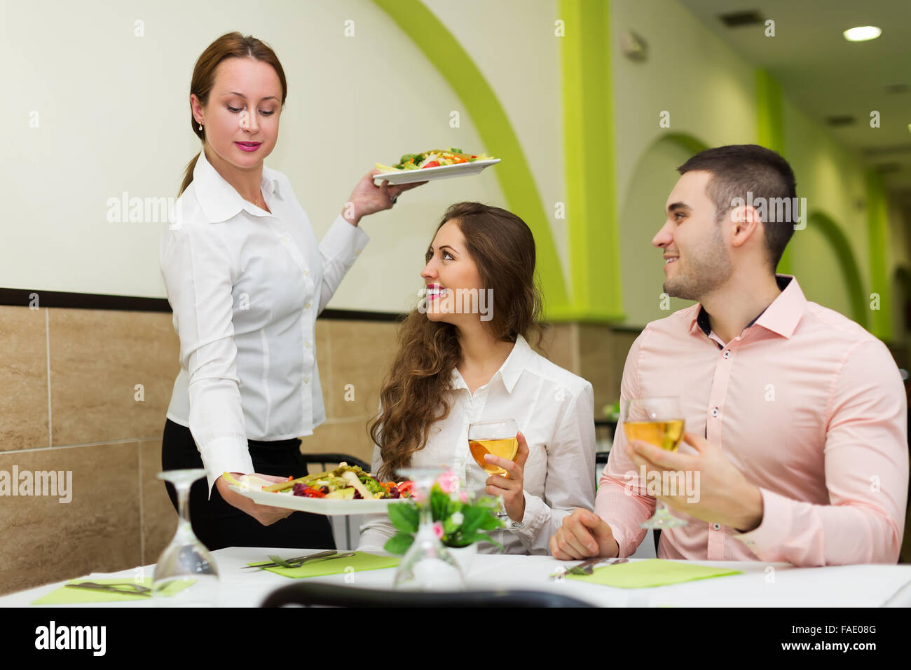 Positive waitress brings plate with prepared food to visitors table ...