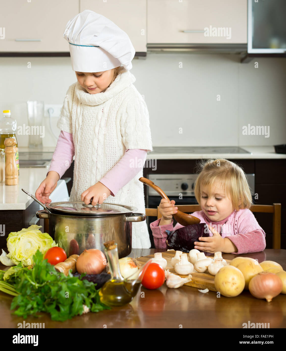 Little girls learn how to prepare a meal in the kitchen wearing a chef ...