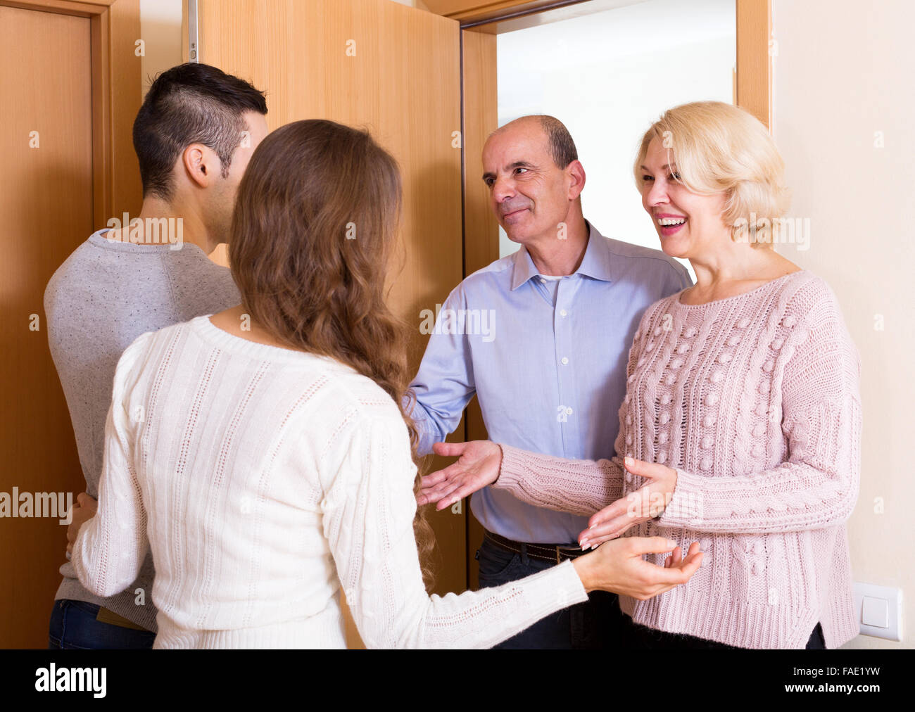 Positive young couple inviting elderly parents to come inside Stock ...