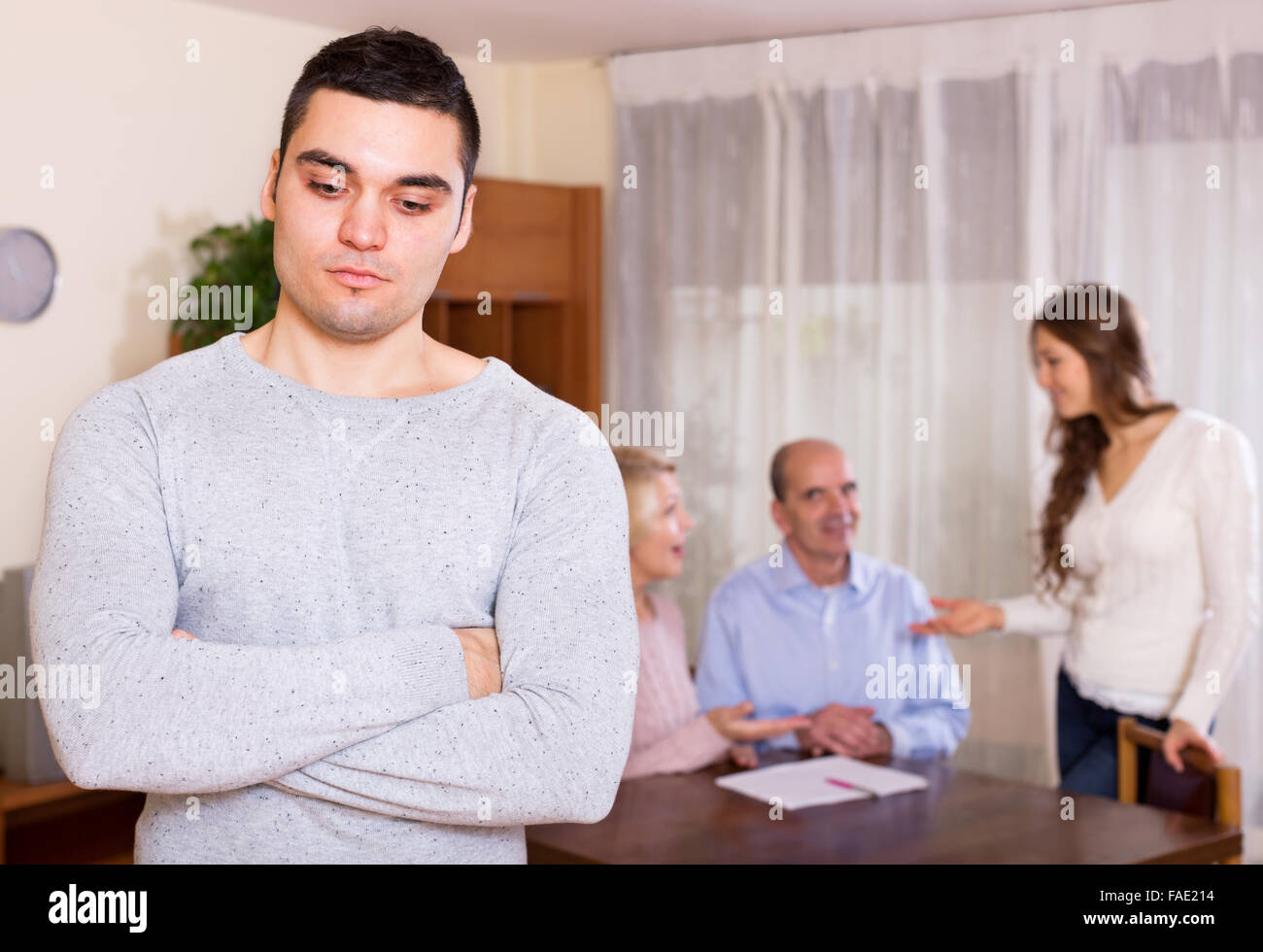Sad young man staying against united family members Stock Photo - Alamy