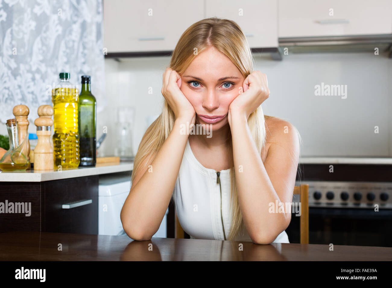Sad woman sitting in kitchen Stock Photo - Alamy
