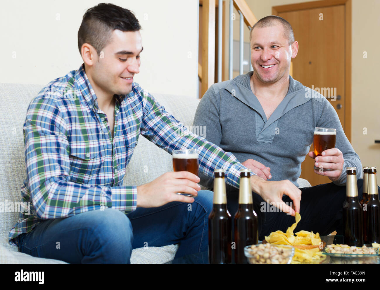 Smiling man sitting at table and drinking beer indoor Stock Photo - Alamy