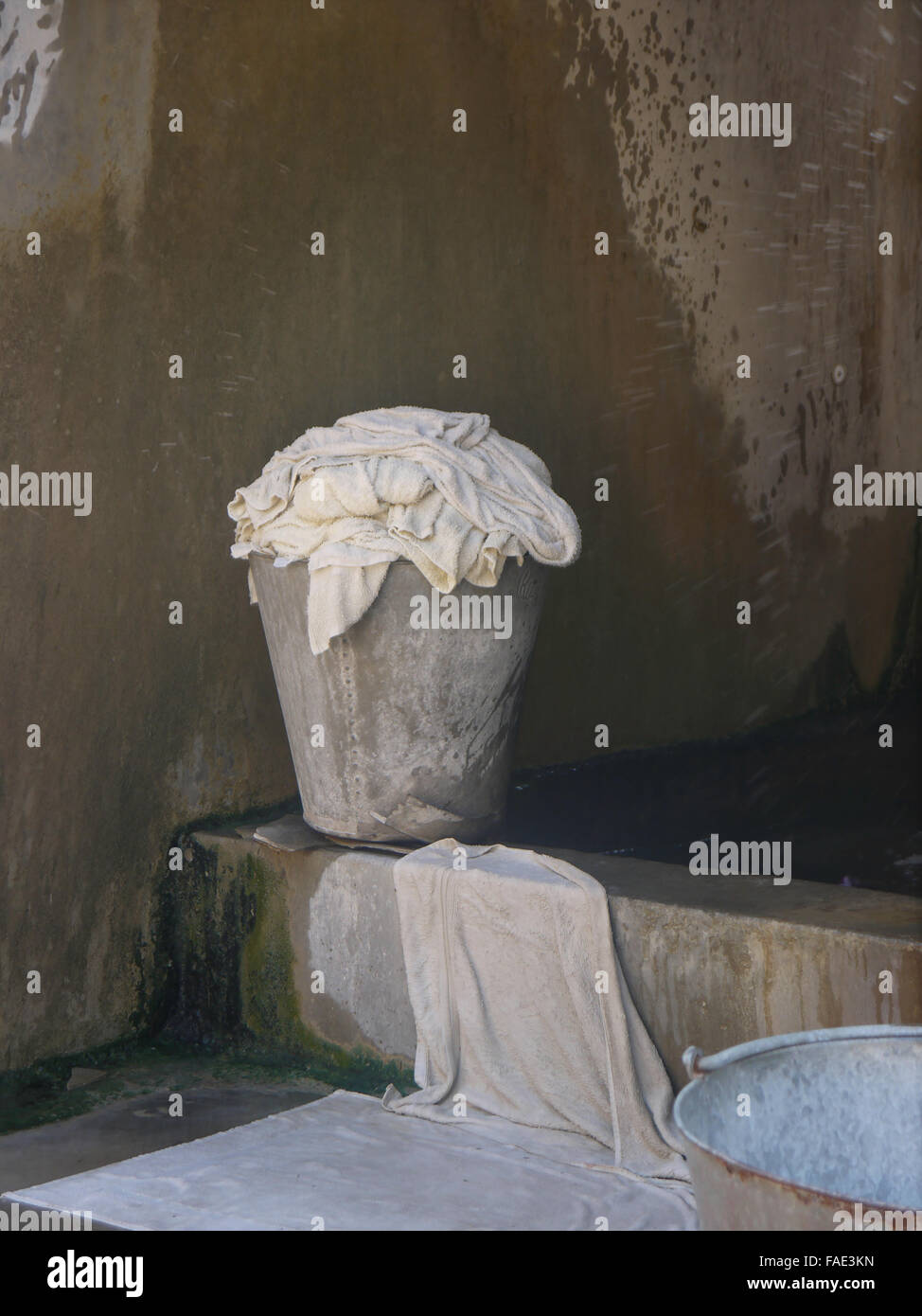 A metal bucket sits on a stone step full of dirty laundry ready to be ...