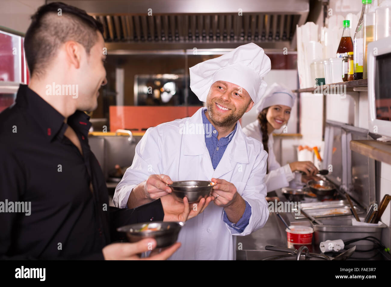 Portrait of happy young male waiter holding dishes and cooks at bistro ...