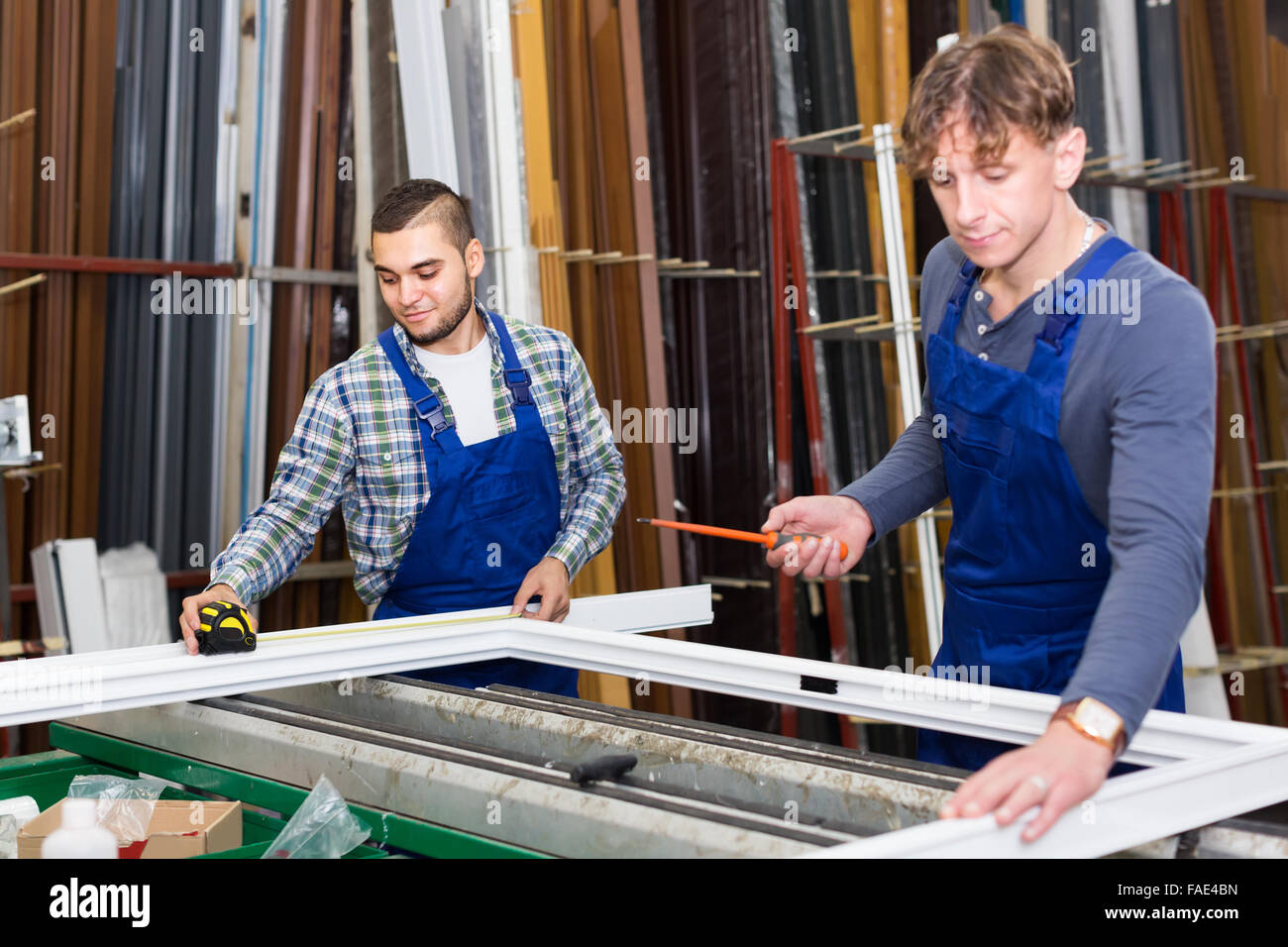 Two workers measuring PVC window profile at stand. Focus on left man ...