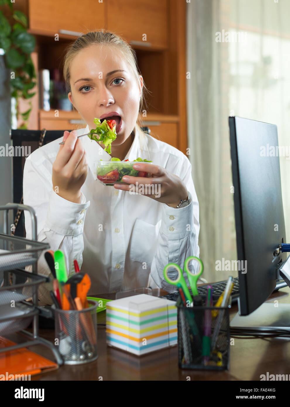 Hangry female worker having vegetables mix at working area Stock Photo ...