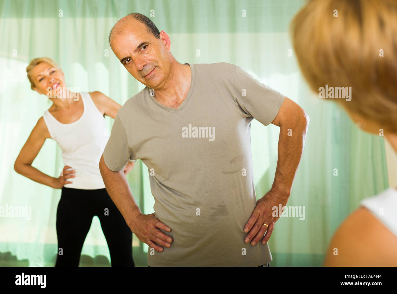 Female trainer showing positive elderly couple how to incline the body ...