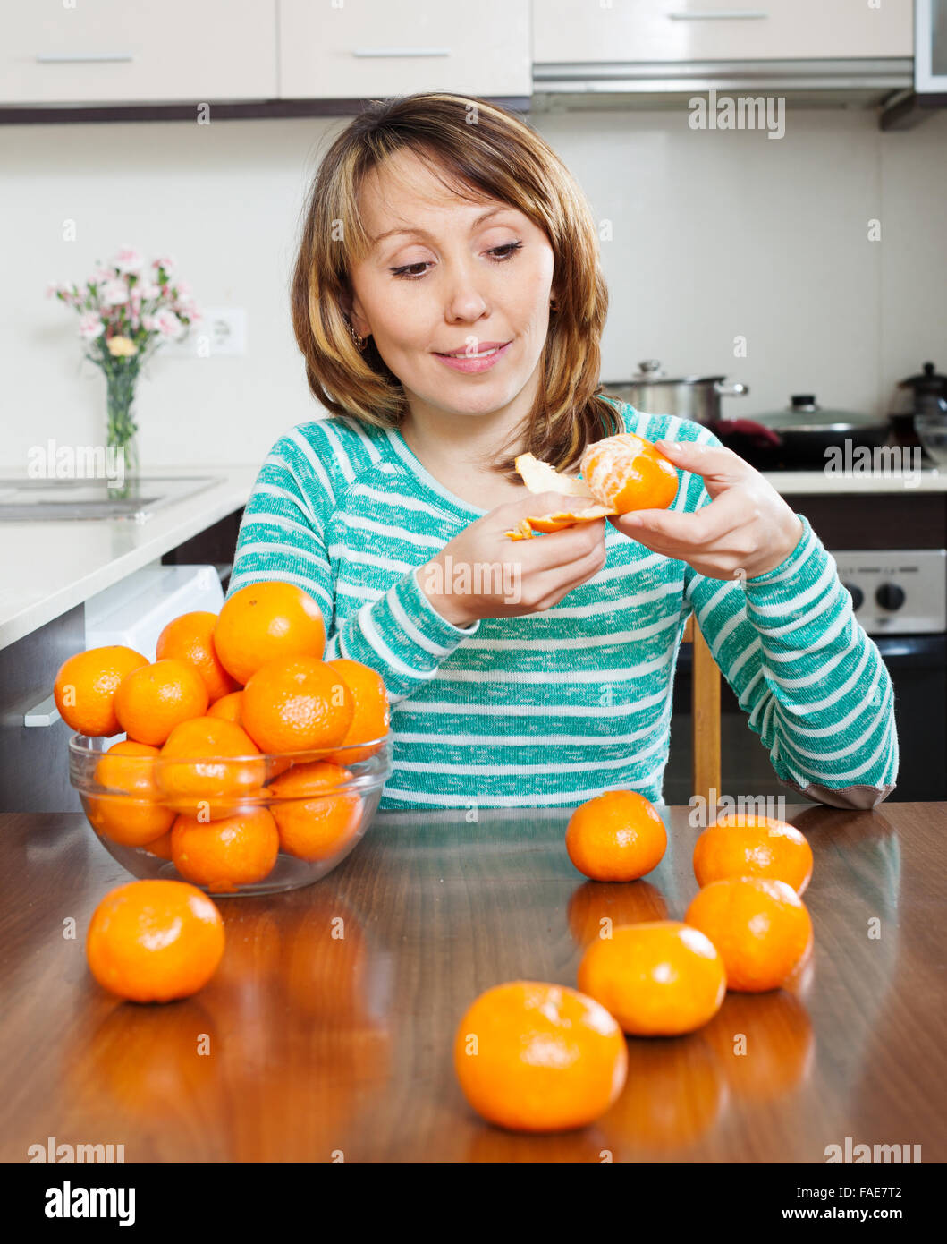 Smiling woman eating mandarins in home kitchen Stock Photo - Alamy