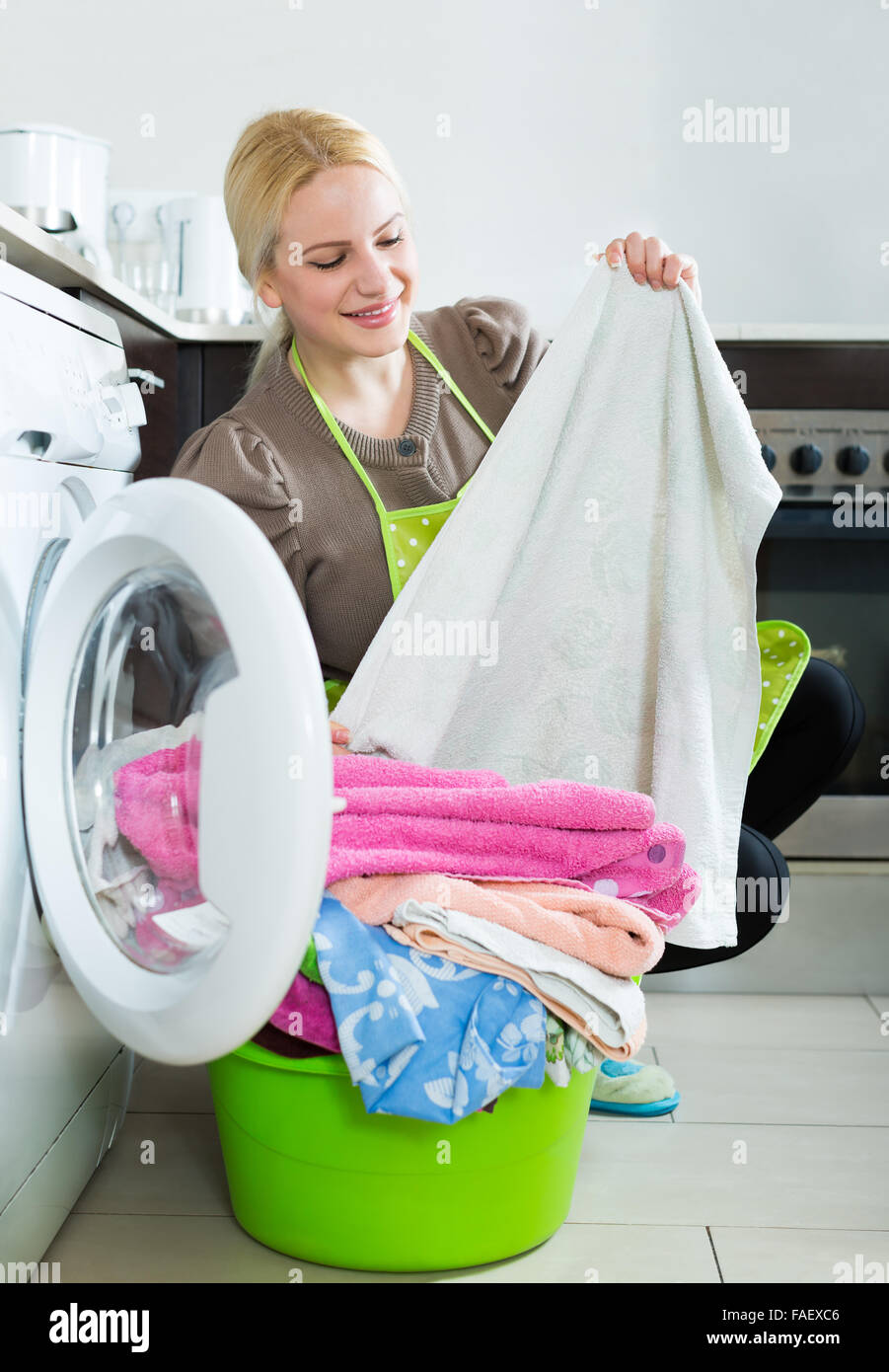 Home laundry. Happy blonde woman loading clothes into a washing machine ...