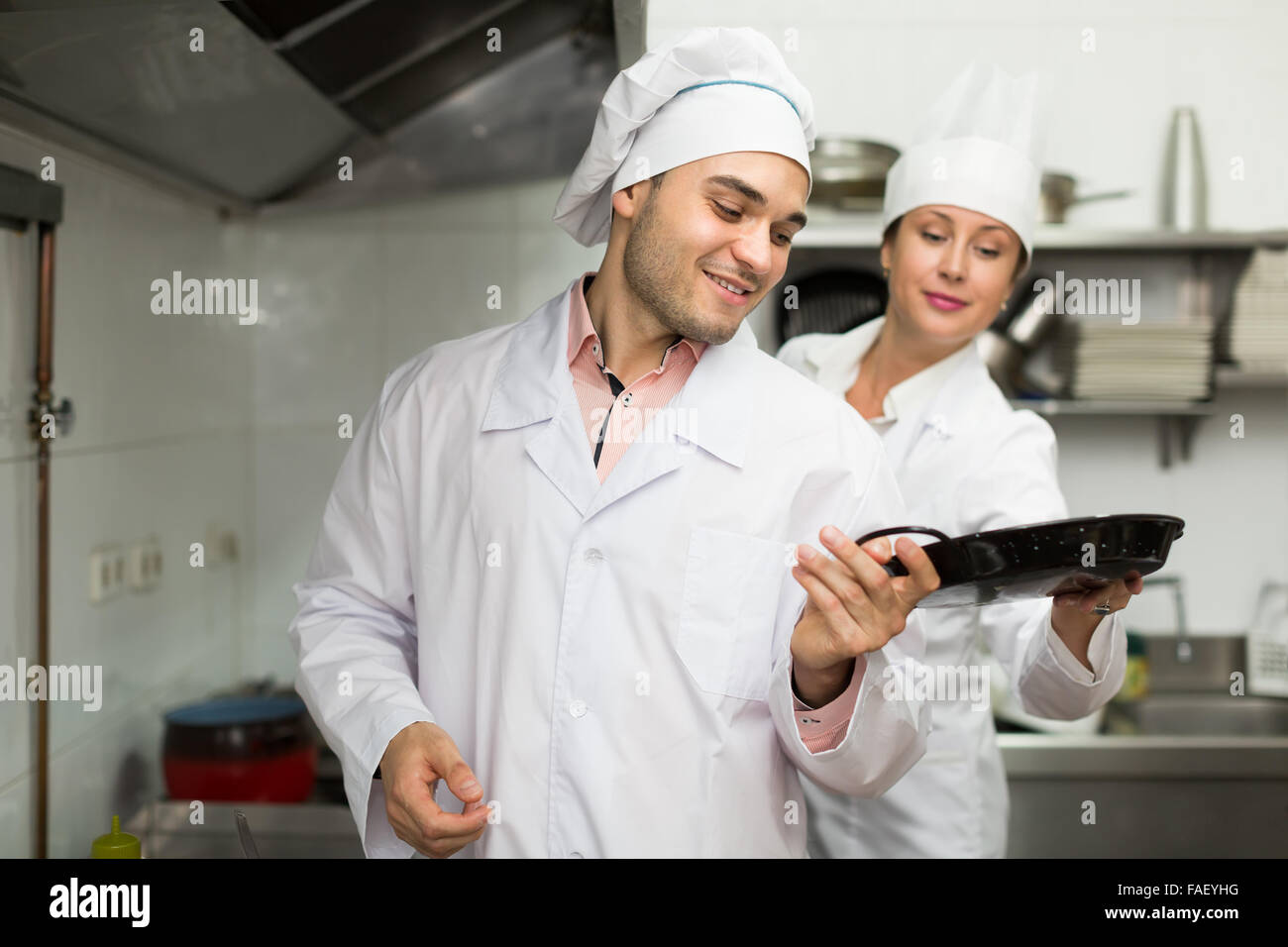 Positive chef with assistant cooking at professional kitchen in the ...