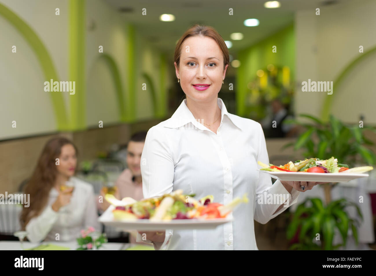 Smiling female waiter serving guests table in restaurant Stock Photo ...