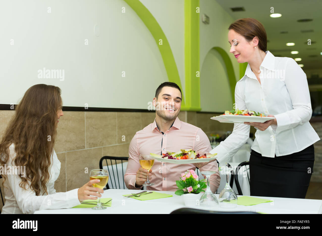 Smiling female waiter serving guests table in restaurant. Focus on man ...