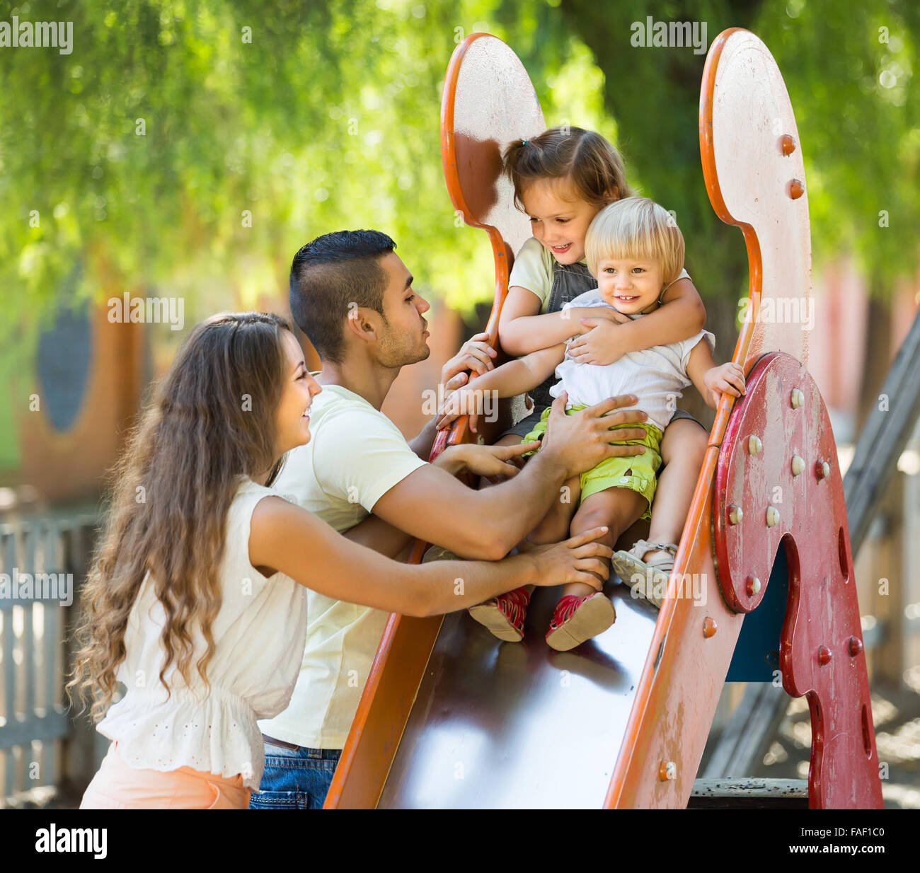 Cheerful parents with two daughters playing at children's slide Stock ...