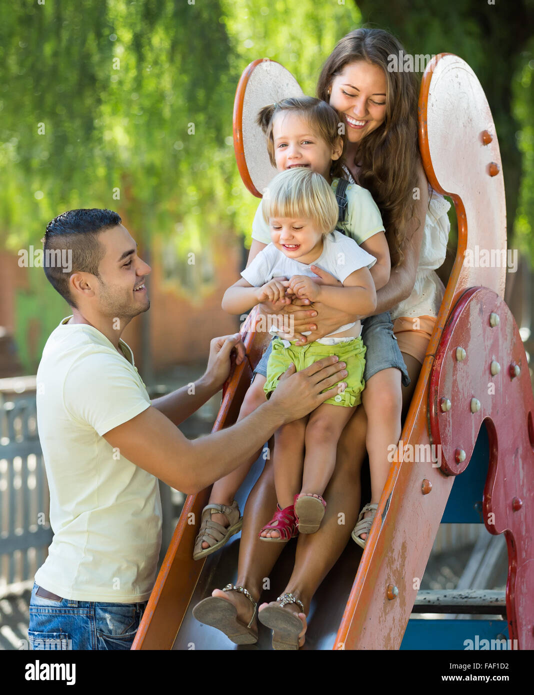 Cheerful young parents with kids at children's playground in summer ...