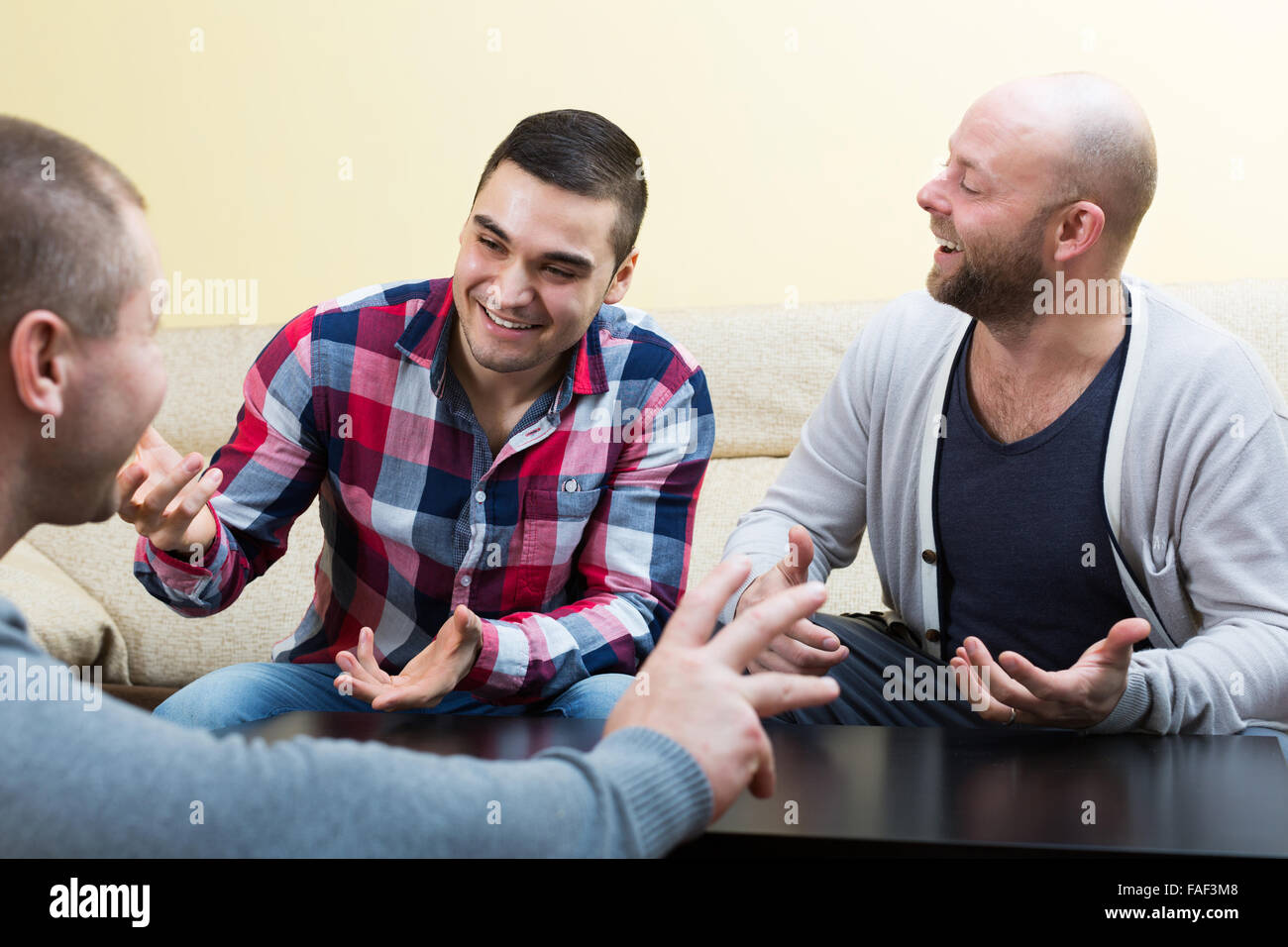 Three adult men talking at living room Stock Photo - Alamy