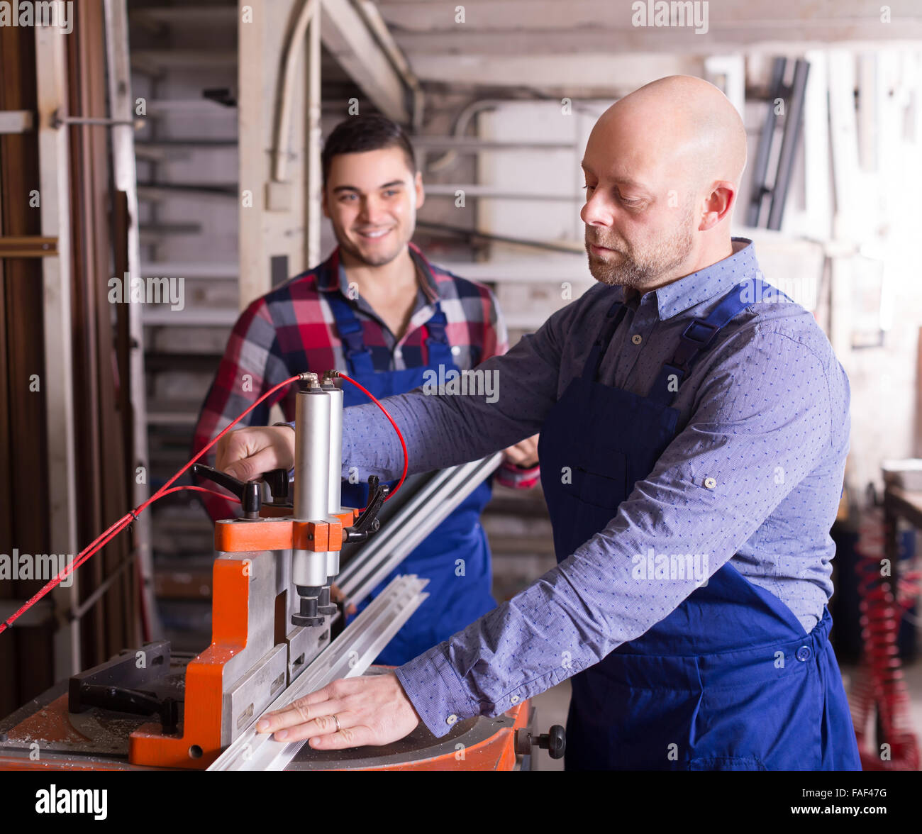 Two positive workmen in uniform working on a machine in PVC shop Stock ...