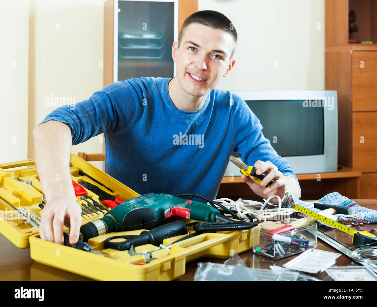 Happy guy sitting by table with tools in toolbox at home Stock Photo ...