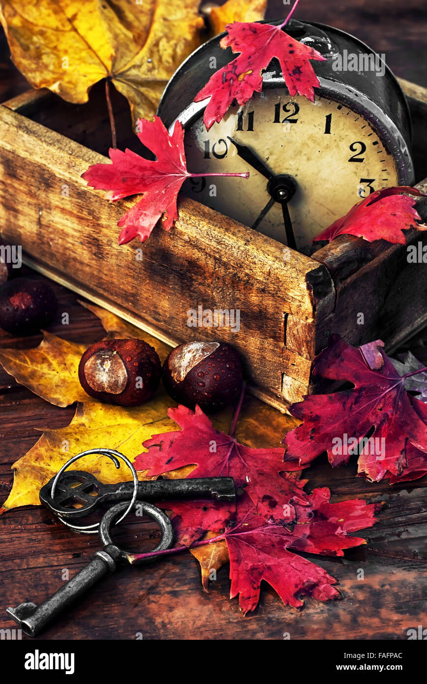 Obsolete alarm clock on wooden background strewn with fallen leaves ...