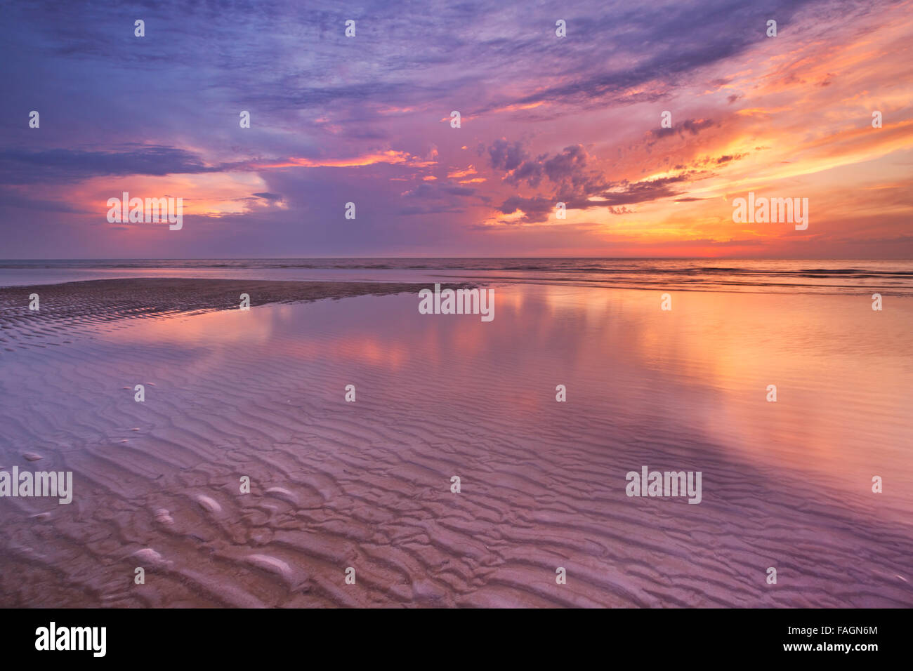Spectacular sunset colours over sea reflected in the water at low tide ...