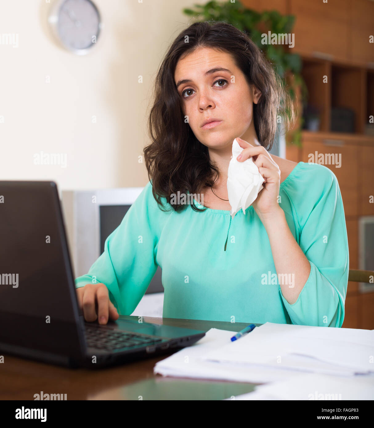 Sad brunette woman with financial documents and laptop at table in home ...