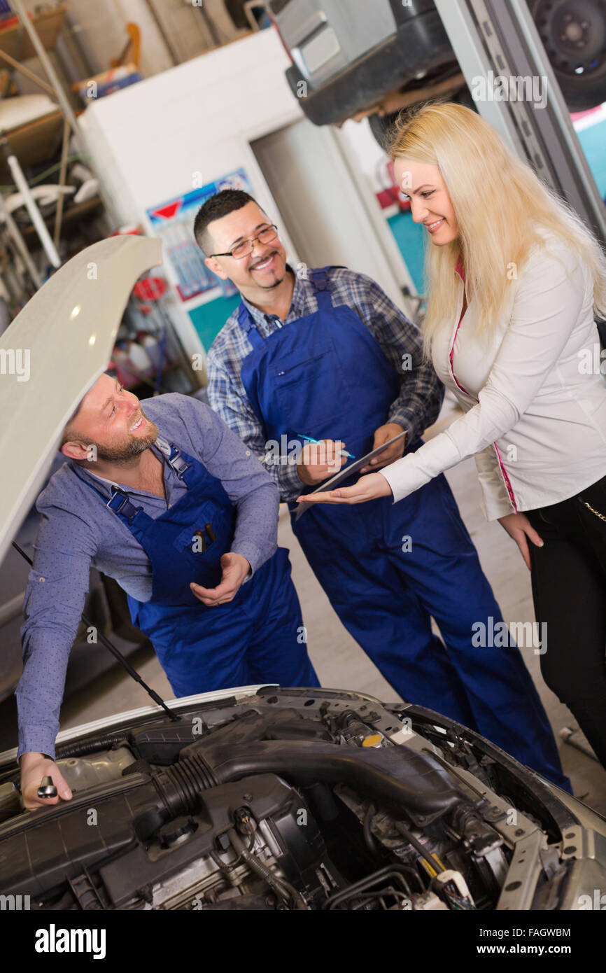 Service crew and positive driver standing near car and smiling indoor ...