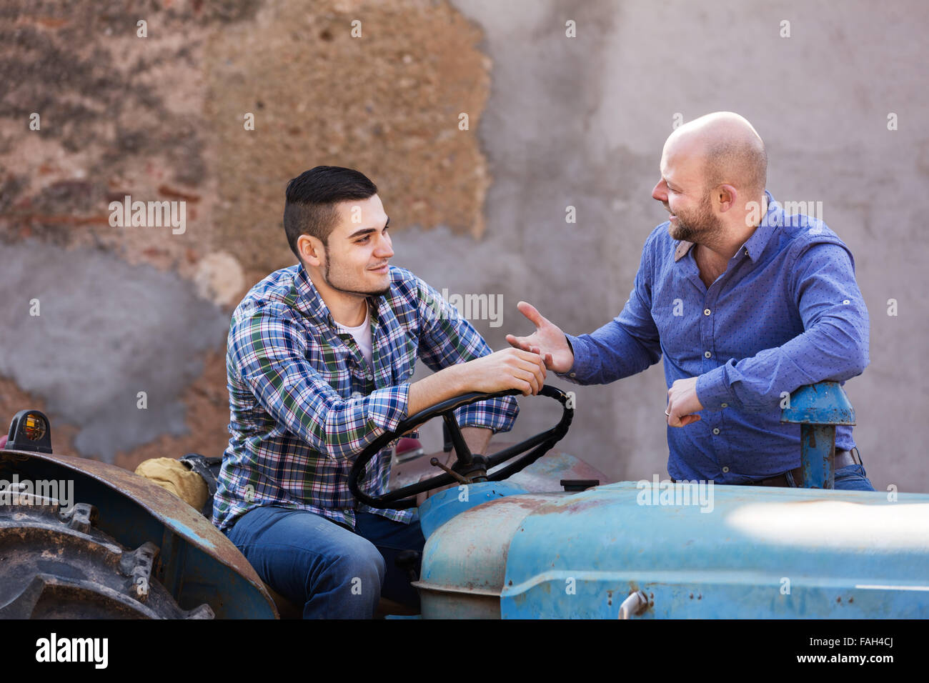 Two happy farmers talking near agricultural machinery at shed Stock ...