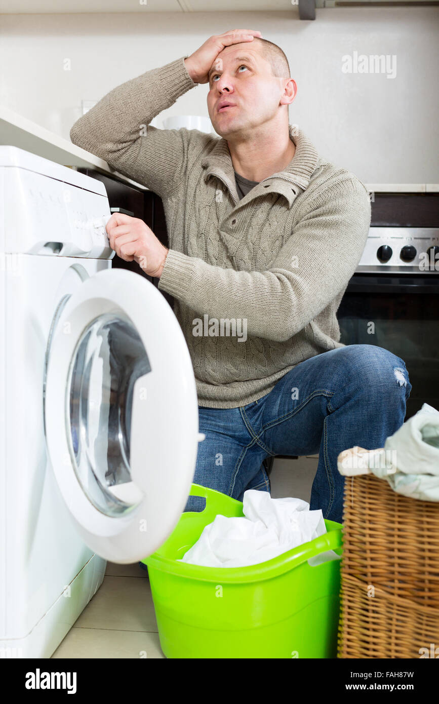 Home laundry. Sad adult guy using washing machine at home Stock Photo ...