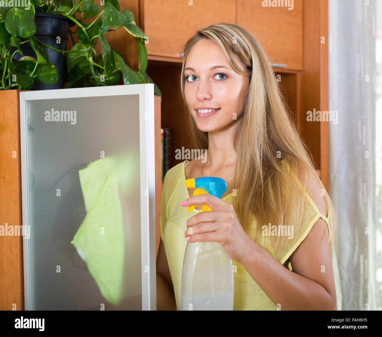 Blonde young girl in yellow cleaning glass door of furniture Stock ...