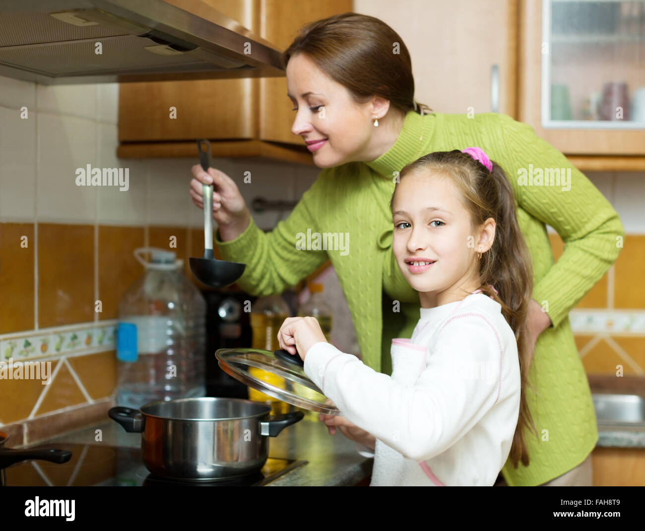 child with her adult mother prepare the soup by the stove in his ...