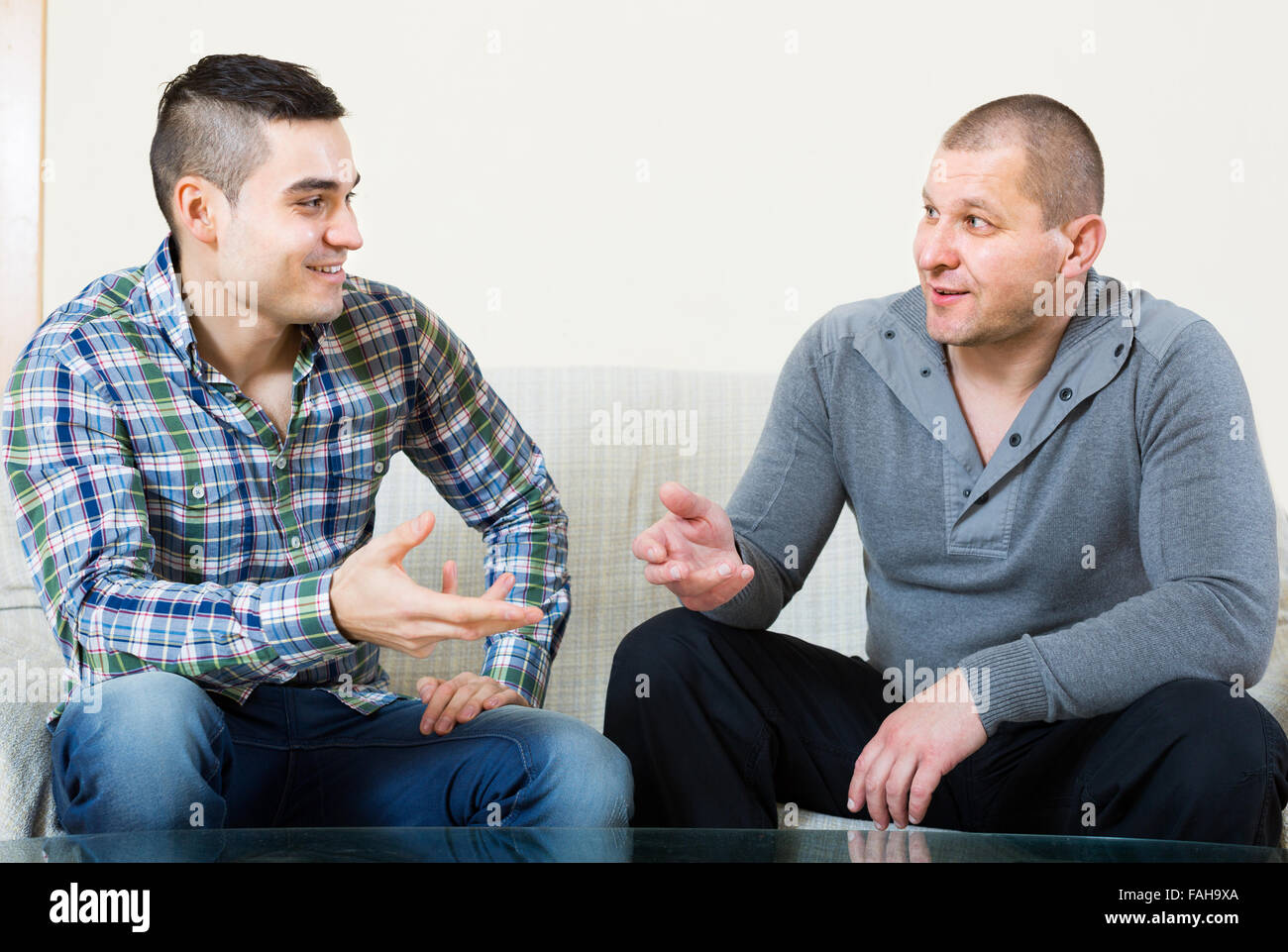 Two smiling buddies relaxing on sofa and chatting in home interior ...