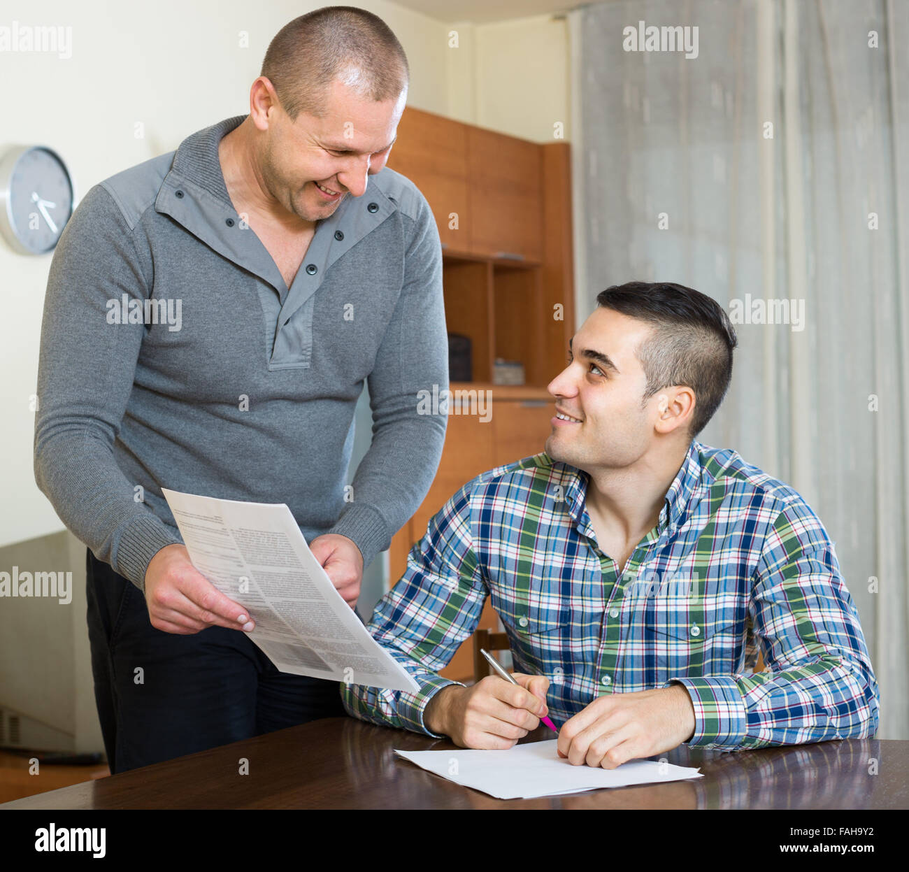 Smiling adult man helping his friend to fill papers at home Stock Photo ...