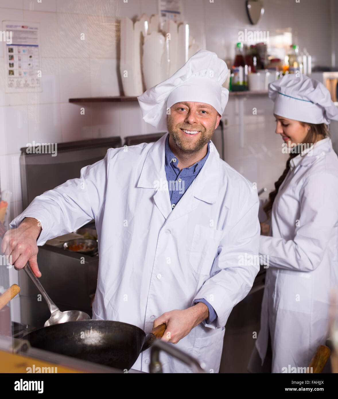 Portrait of positive smiling chef with female assistant at kitchen in ...