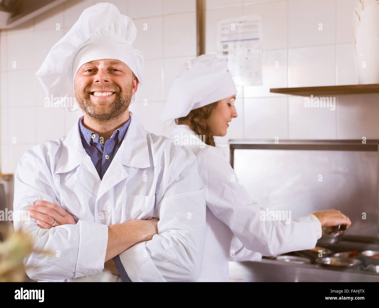 Portrait of positive smiling chef with young female assistant at ...
