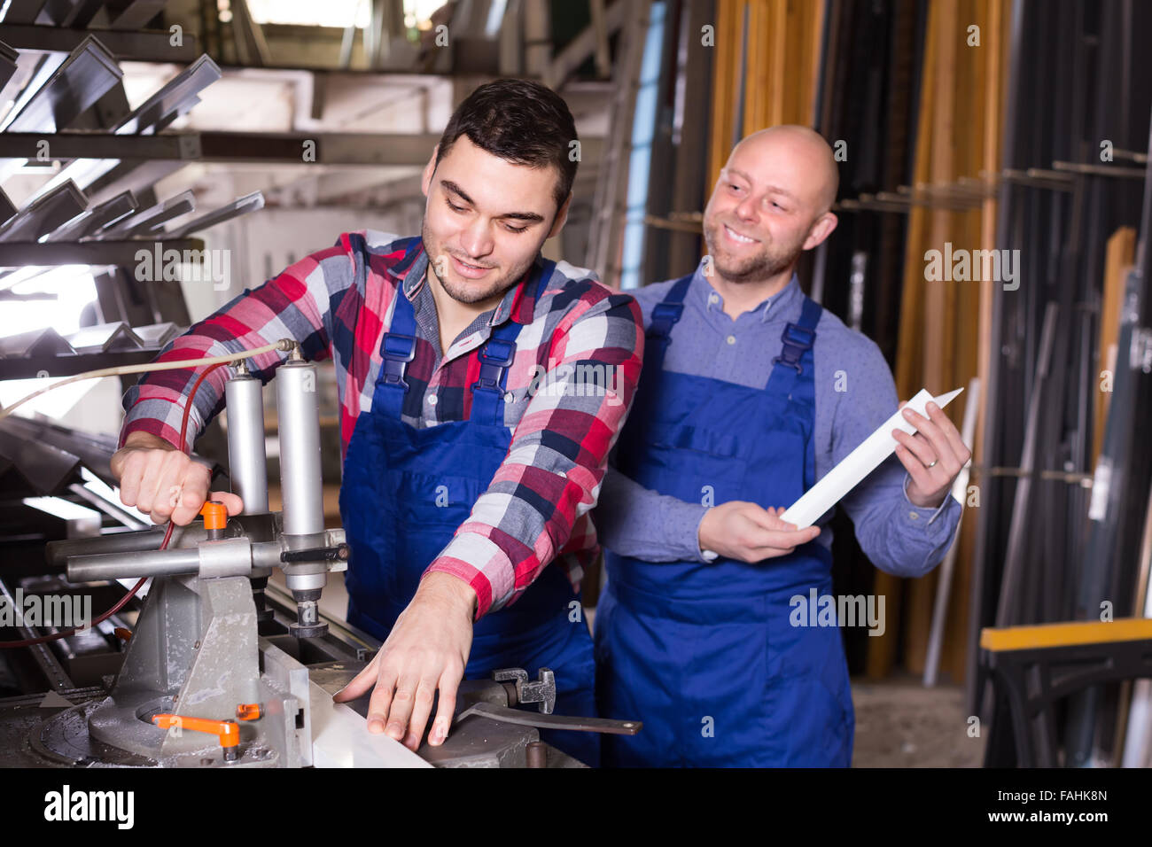 Two positive cheerful workers in uniform working on a machine in PVC ...