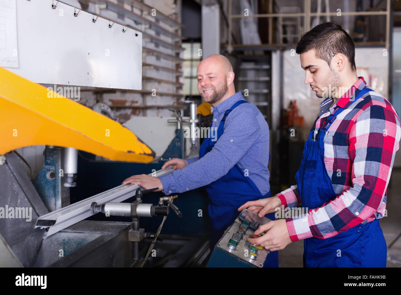 Two adult men in uniform working on machine in PVC shop Stock Photo - Alamy