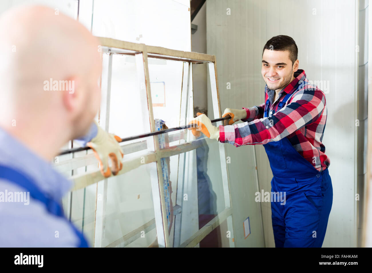Two production workers in coverall working with different PVC window ...