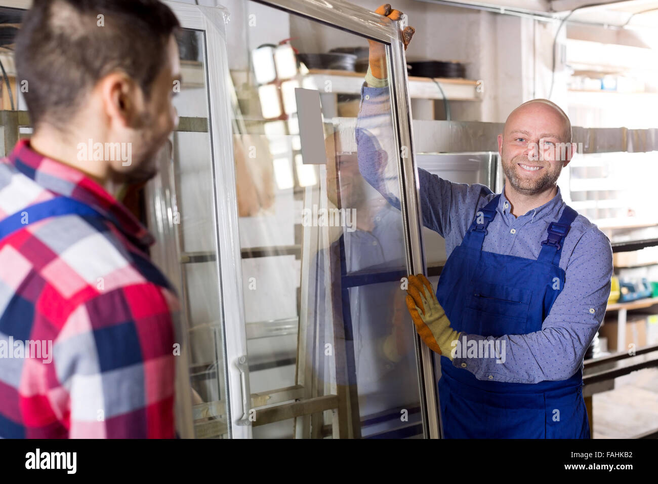 Two workmen in blue overalls with windows production at modern factory ...