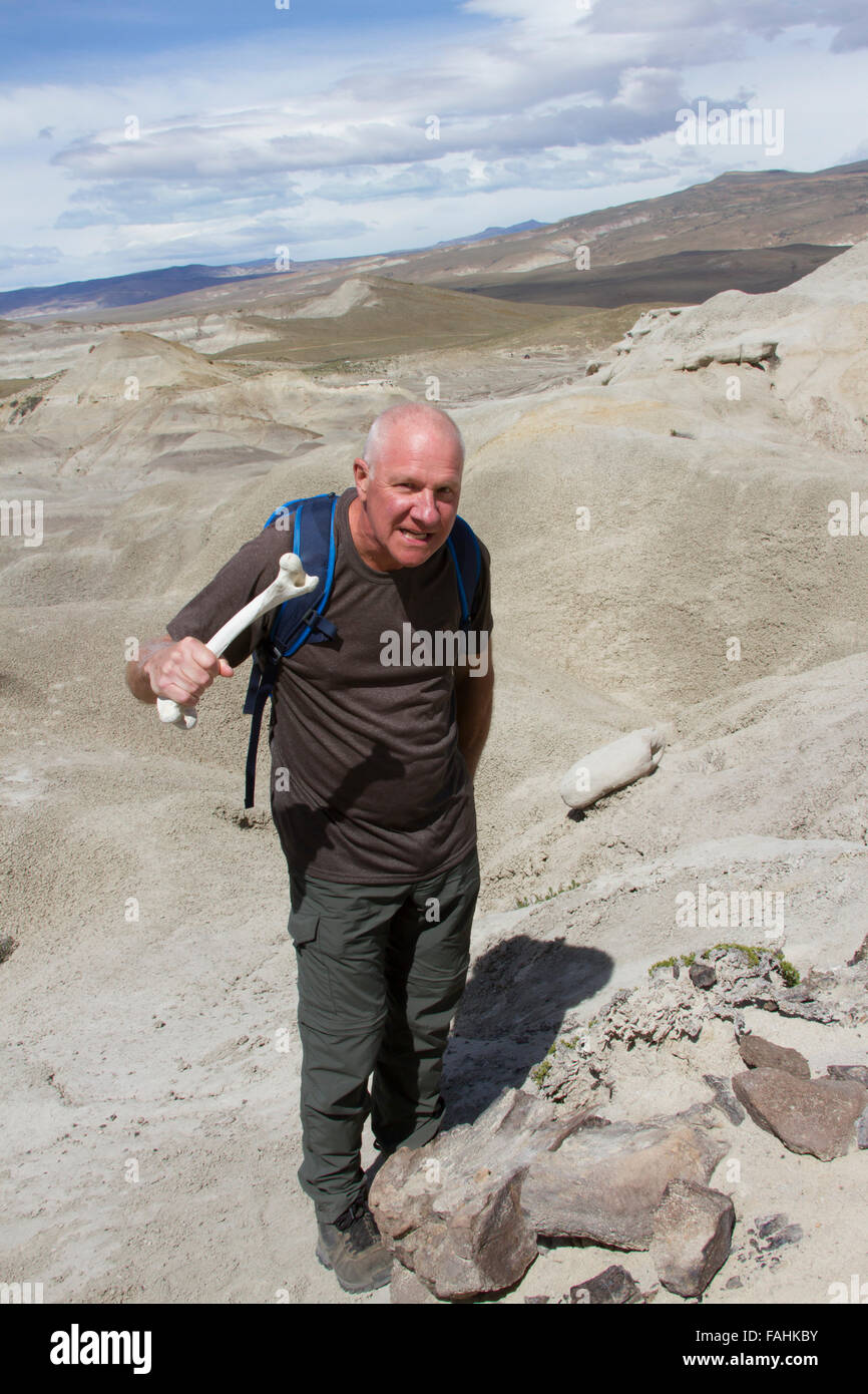 Man posing with guanaco bone standing over fossilized dinosaur bones in ...