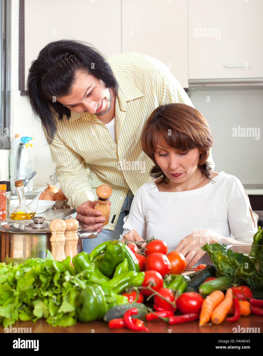 Positive woman and man adding spices or salt to the pot and in kitchen ...