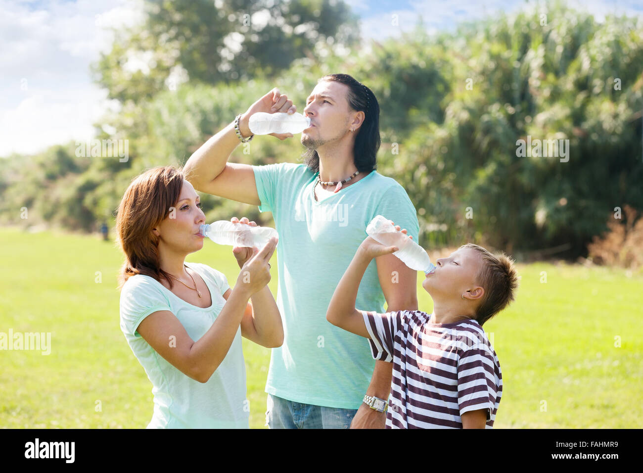 parents with teenager son drinking water from plastic bottles in summer ...