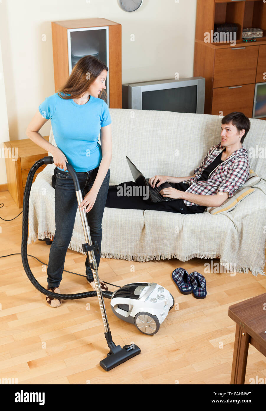 woman doing house cleaning with vaccuum cleaner during man resting over ...