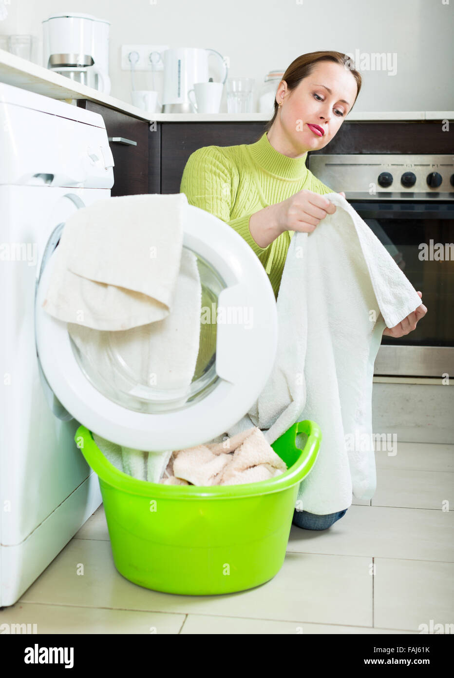 unhappy woman in green doing laundry with washing machine at home kitchen Stock Photo - Alamy