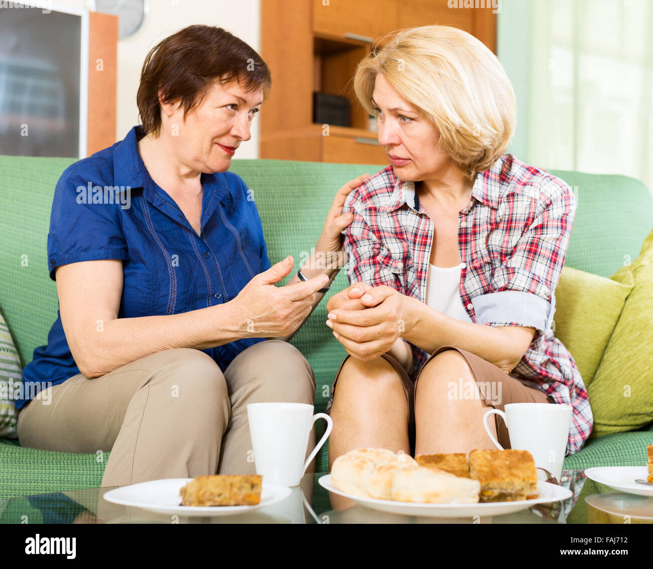 Two sad aged women talking on couch at home Stock Photo - Alamy
