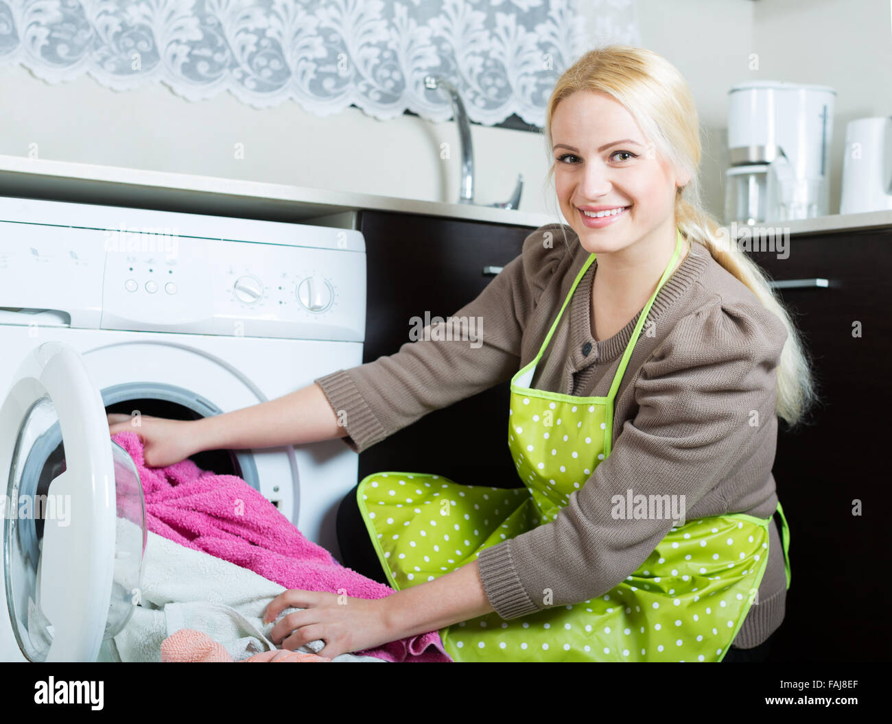 Home laundry. Happy blonde woman loading clothes into the washing ...