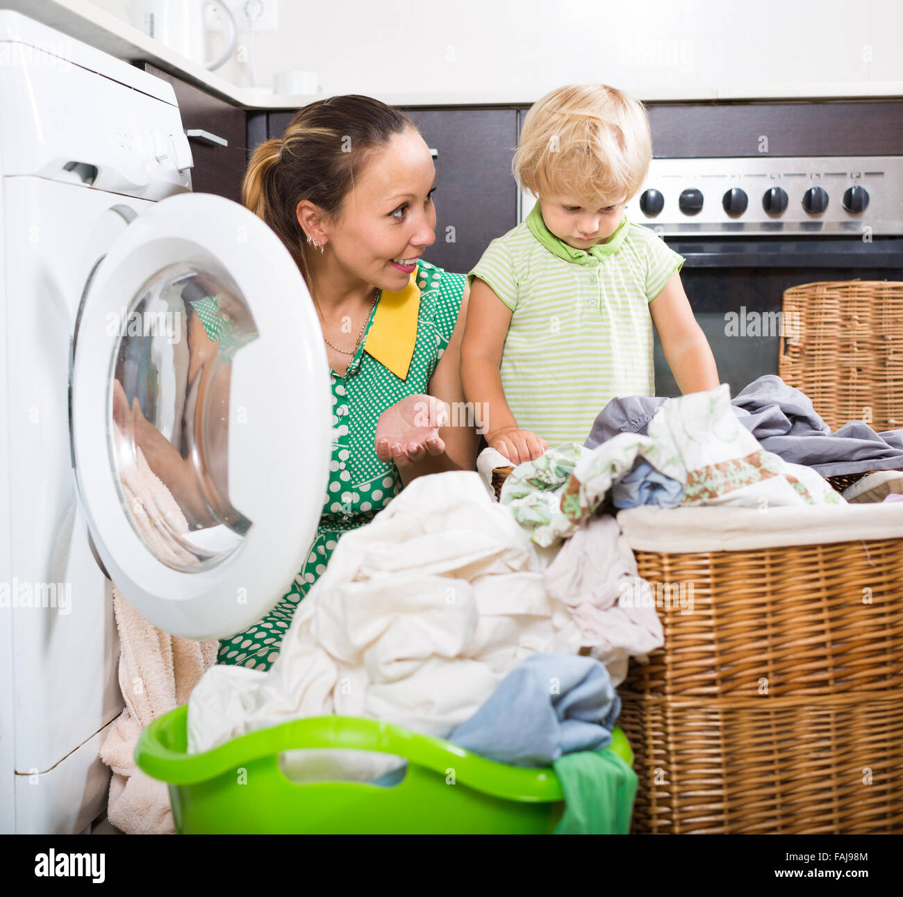 Home laundry. Smiling mother with little child using washing machine at ...